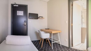 Quarto de hotel com cama, escrivaninha, cadeira, TV fixada na parede e porta com aviso.