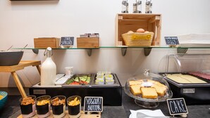 Buffet de café da manhã com seções identificadas para iogurte, manteiga, ovos, bolo e geleia.