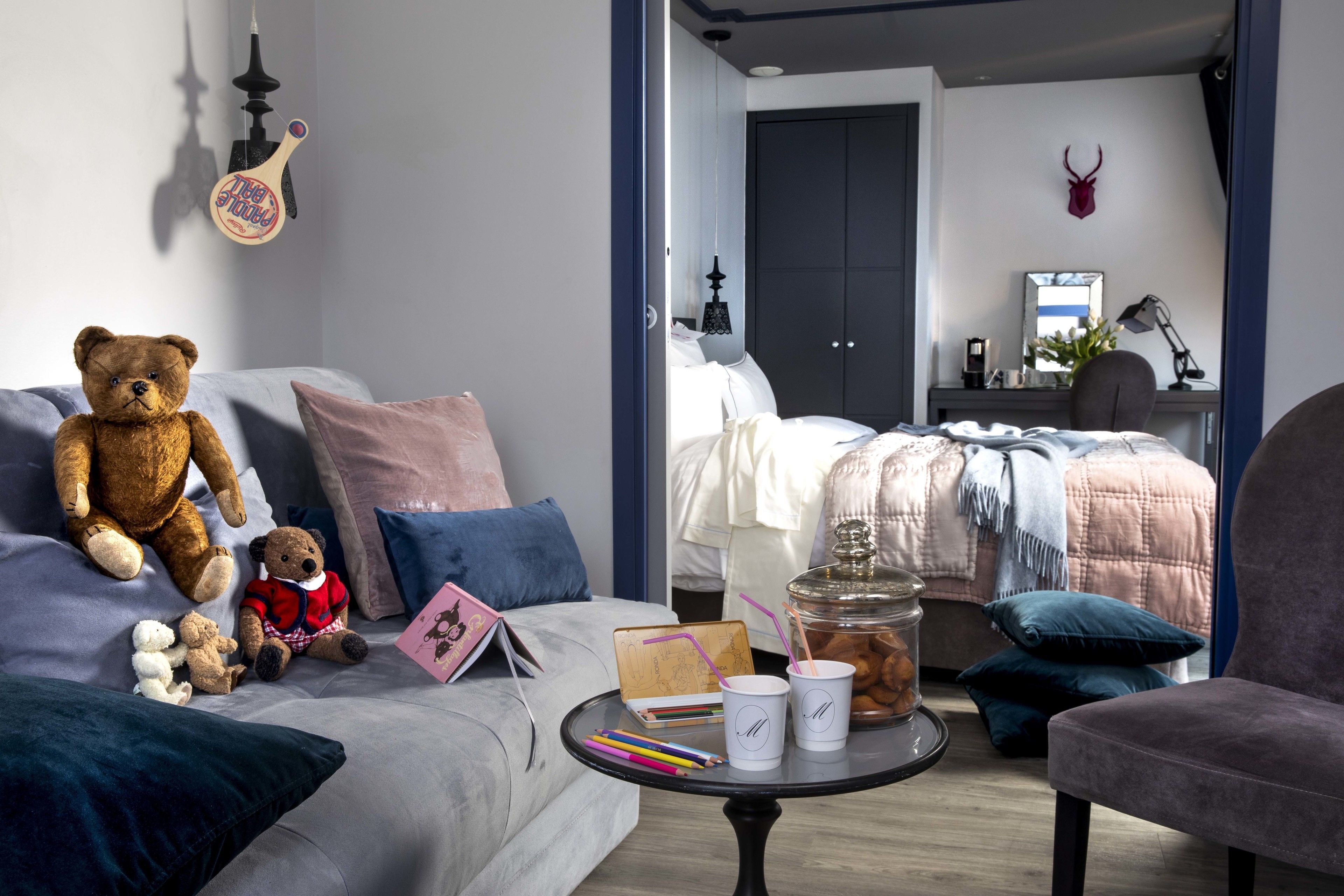 Quarto aconchegante com cama, escrivaninha e cadeira. Há bichos de pelúcia na cama e uma luminária na escrivaninha.