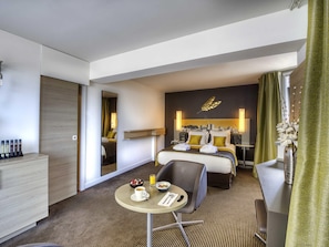 Quarto de hotel com cama, escrivaninha, cadeira, pequena mesa com café da manhã e banheiro.