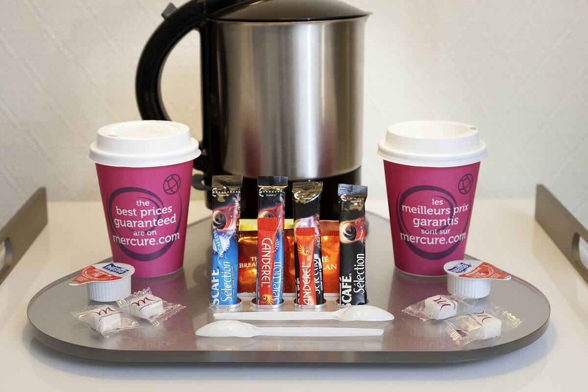 Estação de café com cafeteira, duas chávenas descartáveis e vários pods de café.