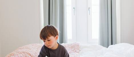Criança lendo um livro em uma cama com colcha xadrez e janela com cortinas.