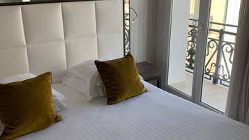 Quarto de hotel com uma cama grande, roupa de cama branca e duas almofadas cor mostarda.