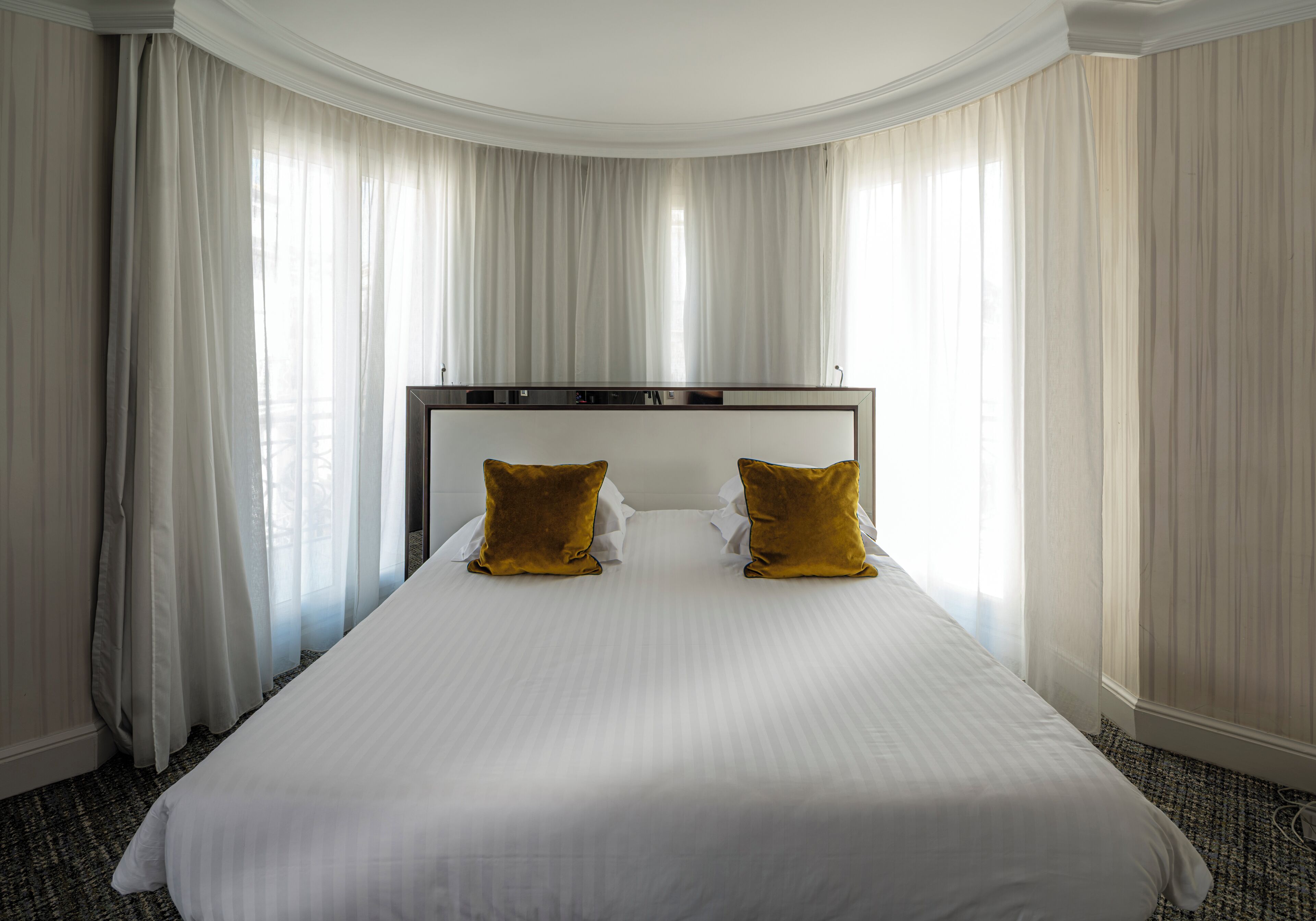 Uma cama grande com lençóis brancos e duas almofadas douradas, teto curvo e cortinas finas.