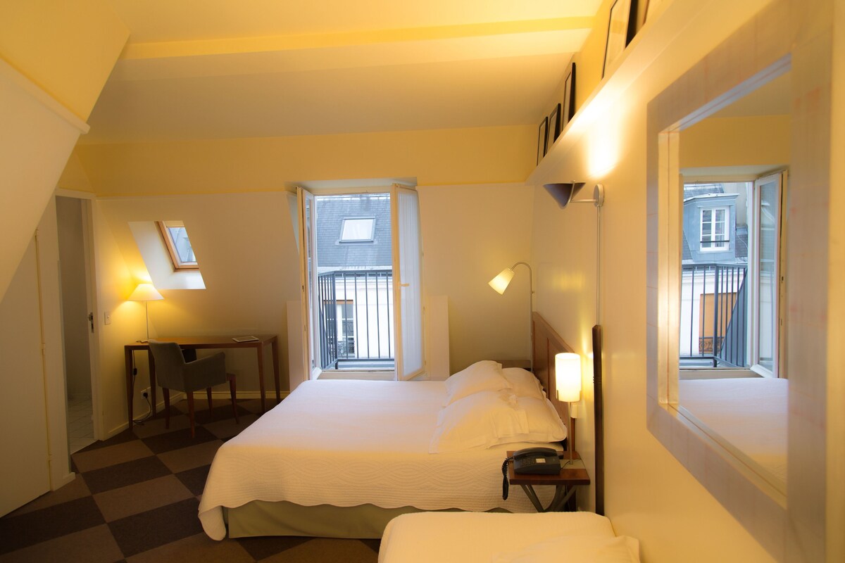 Quarto de hotel com cama, escrivaninha, cadeira, telefone e janela.