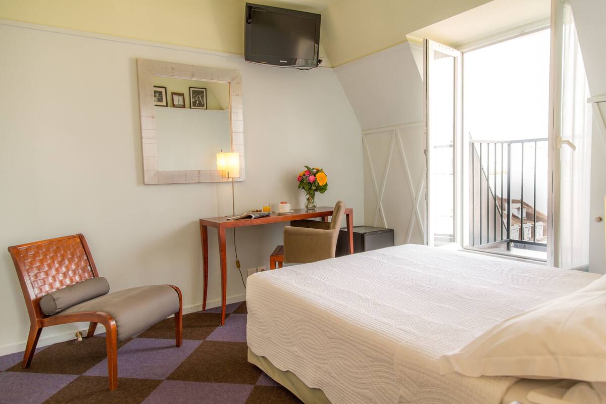 Quarto de hotel com cama, escrivaninha, cadeira, televisão e varanda.