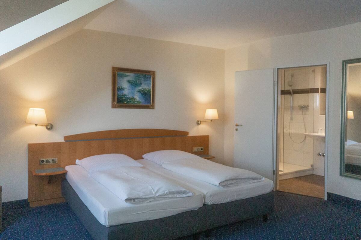 Quarto de hotel com cama de casal, duas mesas de cabeceira, um quadro na parede e área de chuveiro.
