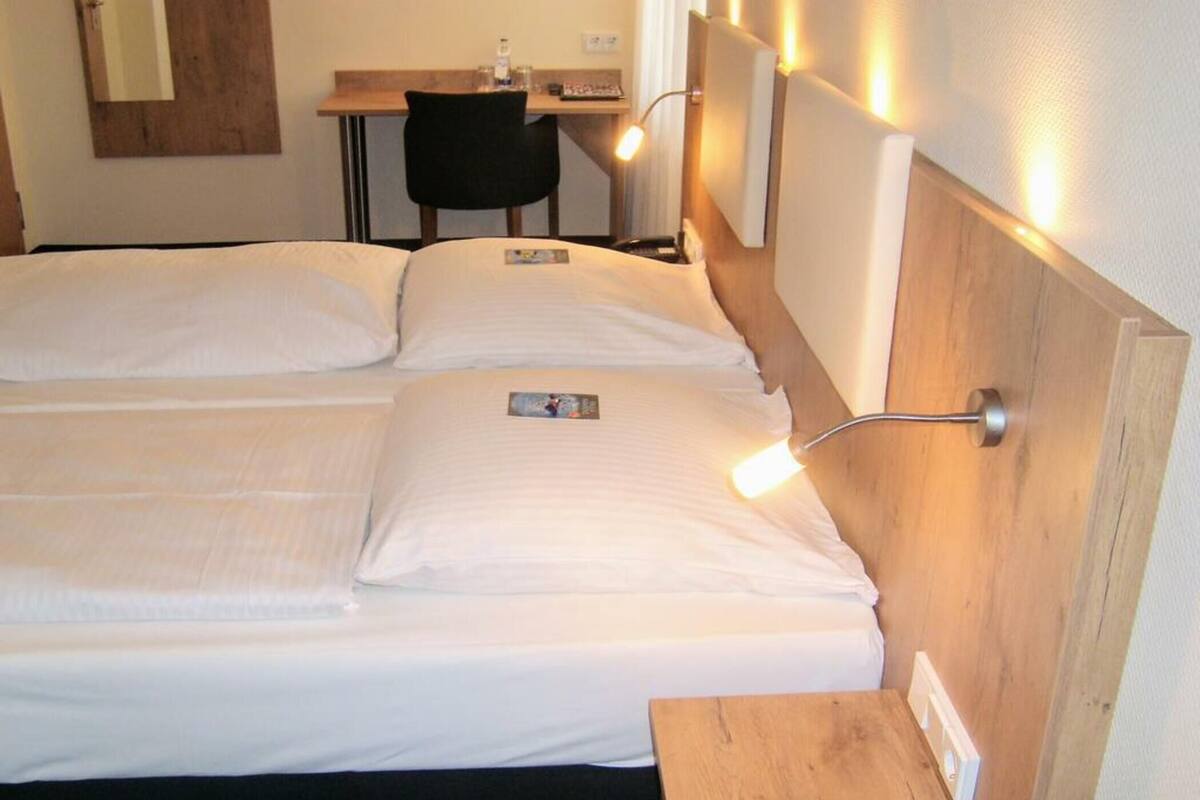 Quarto de hotel com duas camas, uma mesa e uma cadeira.