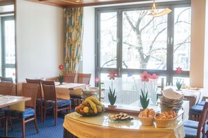 Espaço de refeições com mesas, cadeiras e um buffet de frutas e pão.