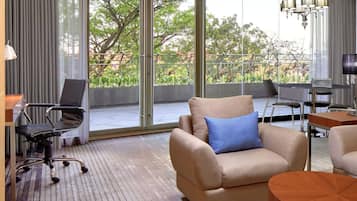 Quarto de hotel moderno com uma grande porta de vidro deslizante que dá para uma varanda, um sofá confortável com um travesseiro azul, uma cadeira de escritório preta, uma mesa de centro de madeira e uma televisão.