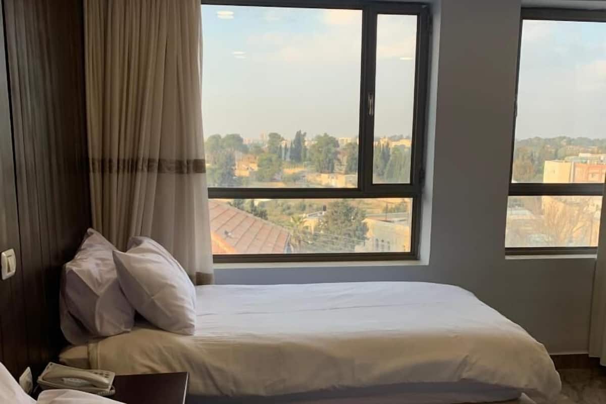 Quarto de hotel com duas camas, uma janela ampla e vista para a cidade, e cortina.