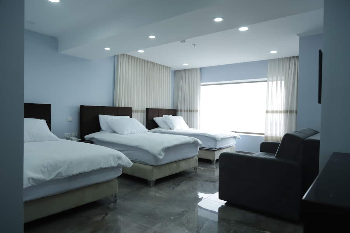Quarto de hotel com três camas, um sofá e uma janela grande com cortinas.
