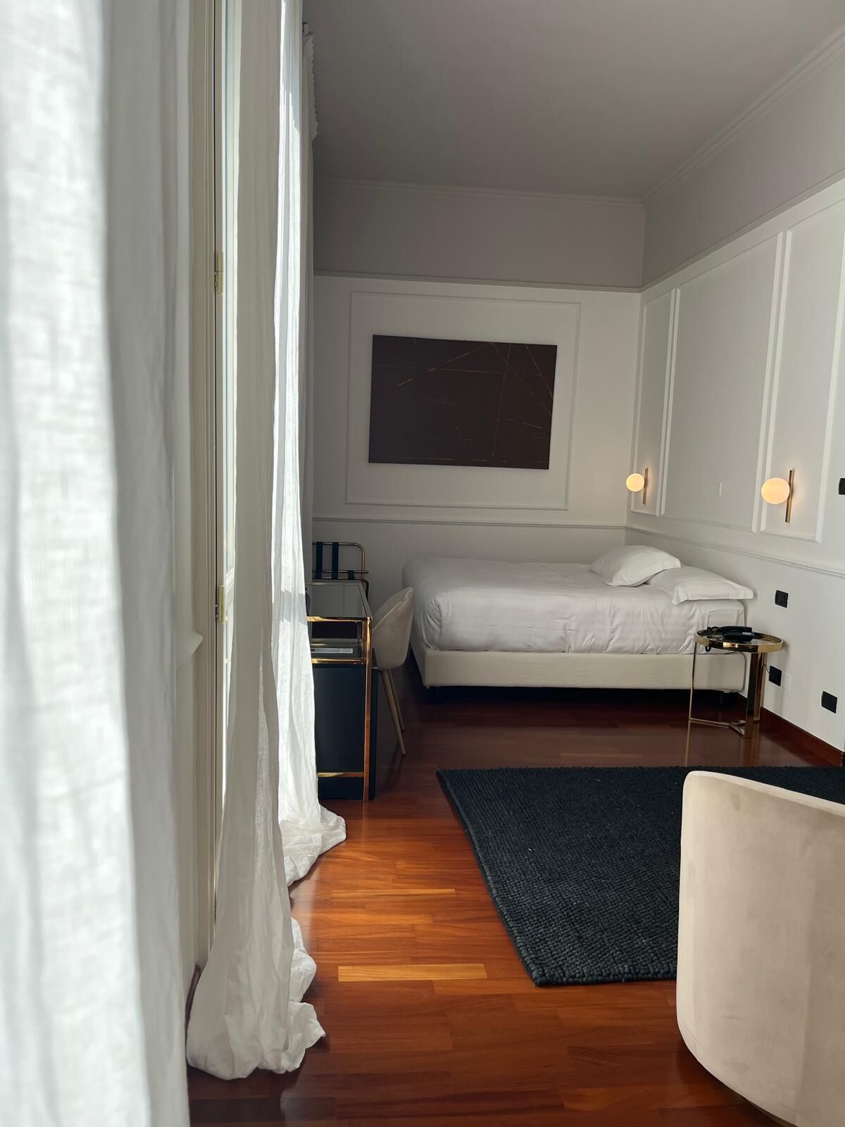 Quarto com cama, mesas de cabeceira, escrivaninha, cadeira, tapete e um quadro na parede.