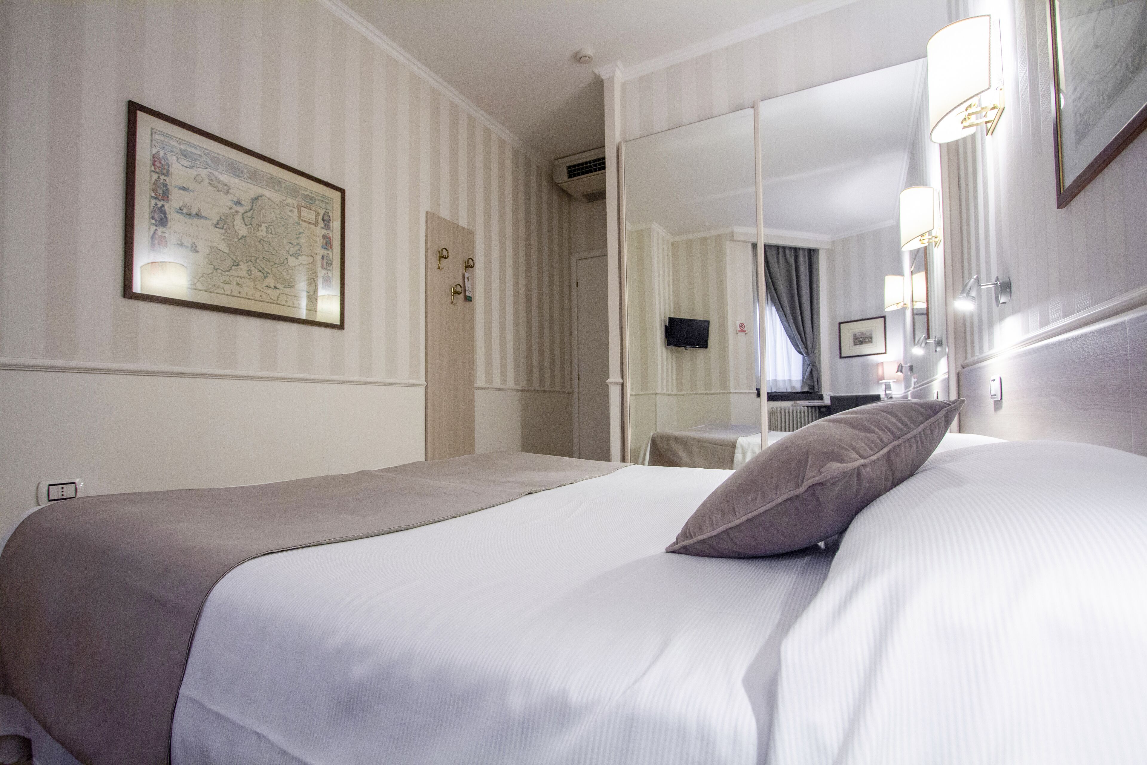 Quarto de hotel com uma cama grande, um espelho, um mapa na parede e uma televisão no canto.