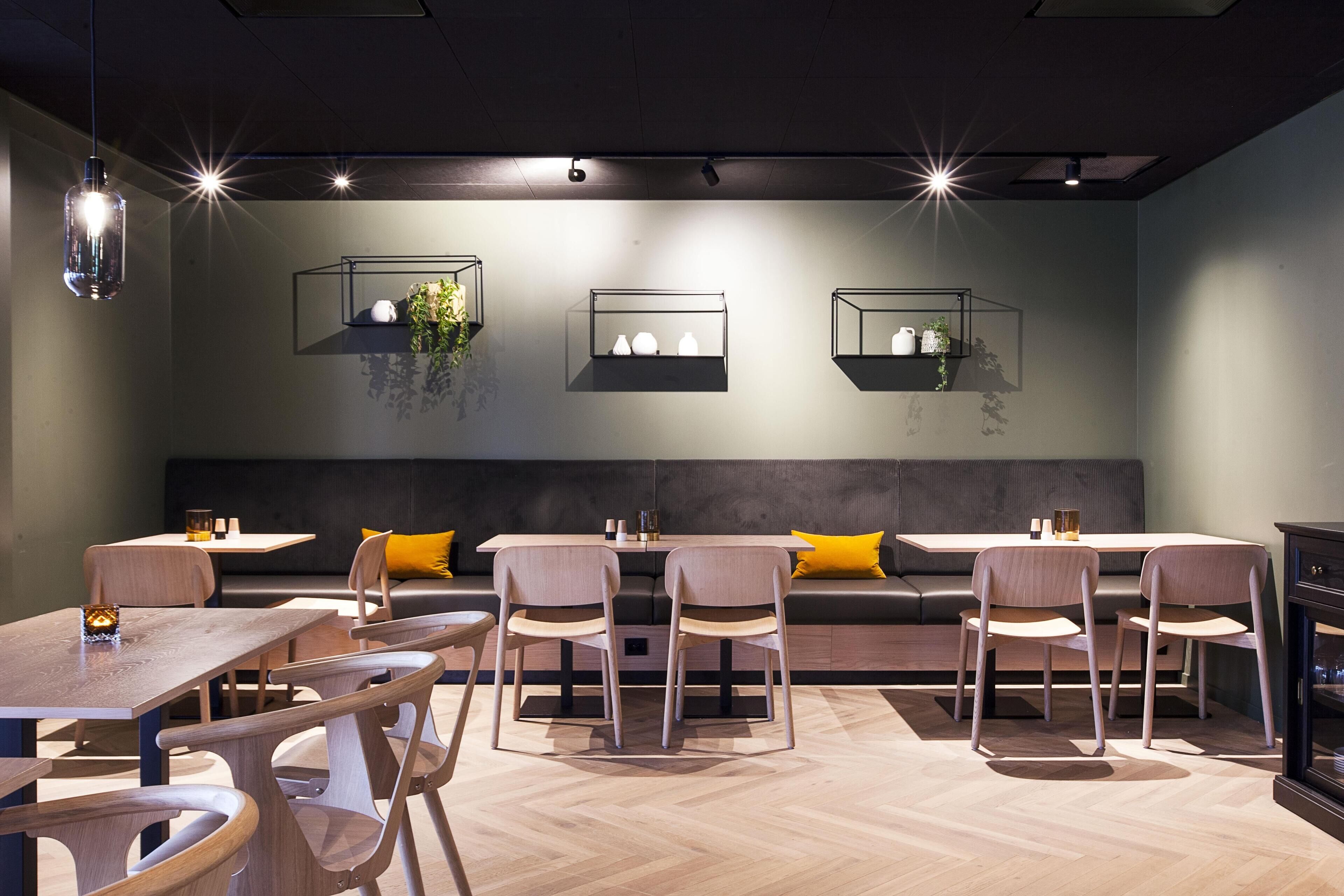 Interior moderno de restaurante com mesas e cadeiras de madeira, um sofá e luminárias pendentes.