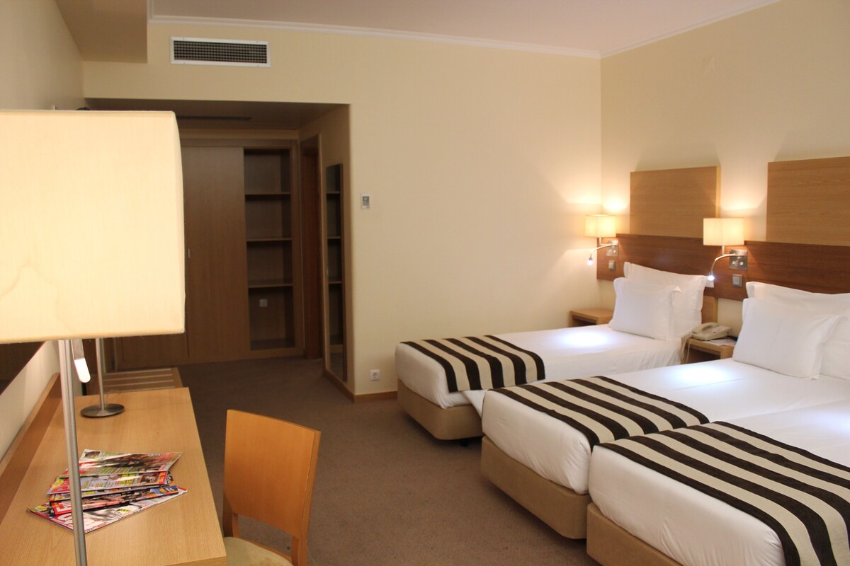 Quarto de hotel com duas camas, uma escrivaninha e uma cadeira.