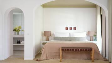 Quarto com uma cama grande, duas luminárias de cabeceira, um banquinho e um espelho.