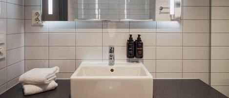 Um banheiro com uma pia branca, um espelho acima e duas garrafas de shampoo na parede.