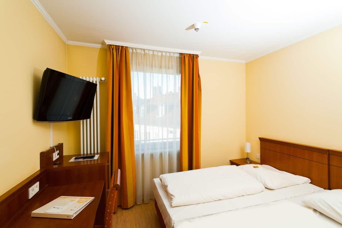 Quarto de hotel com cama, secretária com televisão de tela plana, mesa de cabeceira e janela com cortinas.
