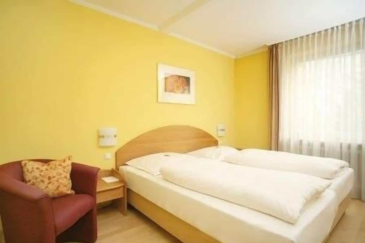 Quarto de hotel com cama, uma cadeira, mesa de cabeceira e um quadro na parede.