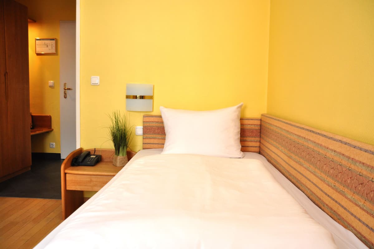 Quarto de hotel com cama, mesa de cabeceira com telefone e planta, e porta com interruptor de luz.