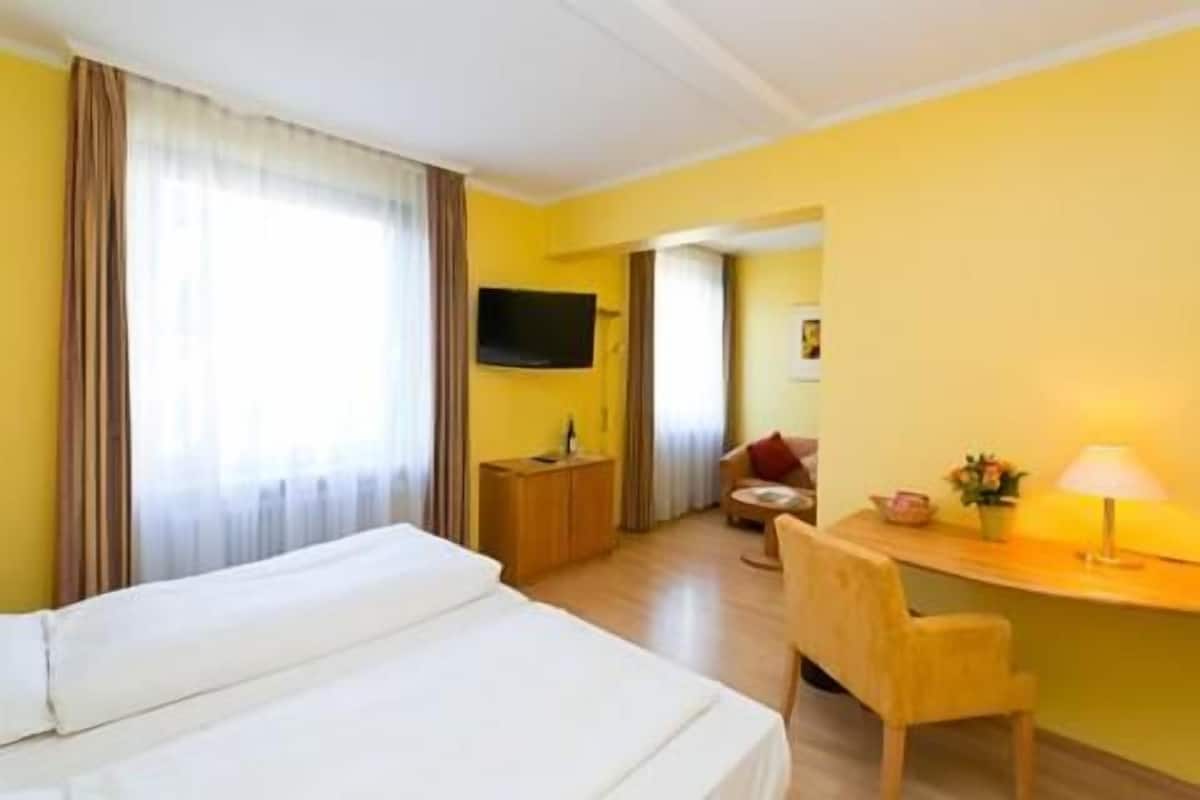 Quarto de hotel com duas camas, uma escrivaninha, uma cadeira, uma televisão e um abajur.