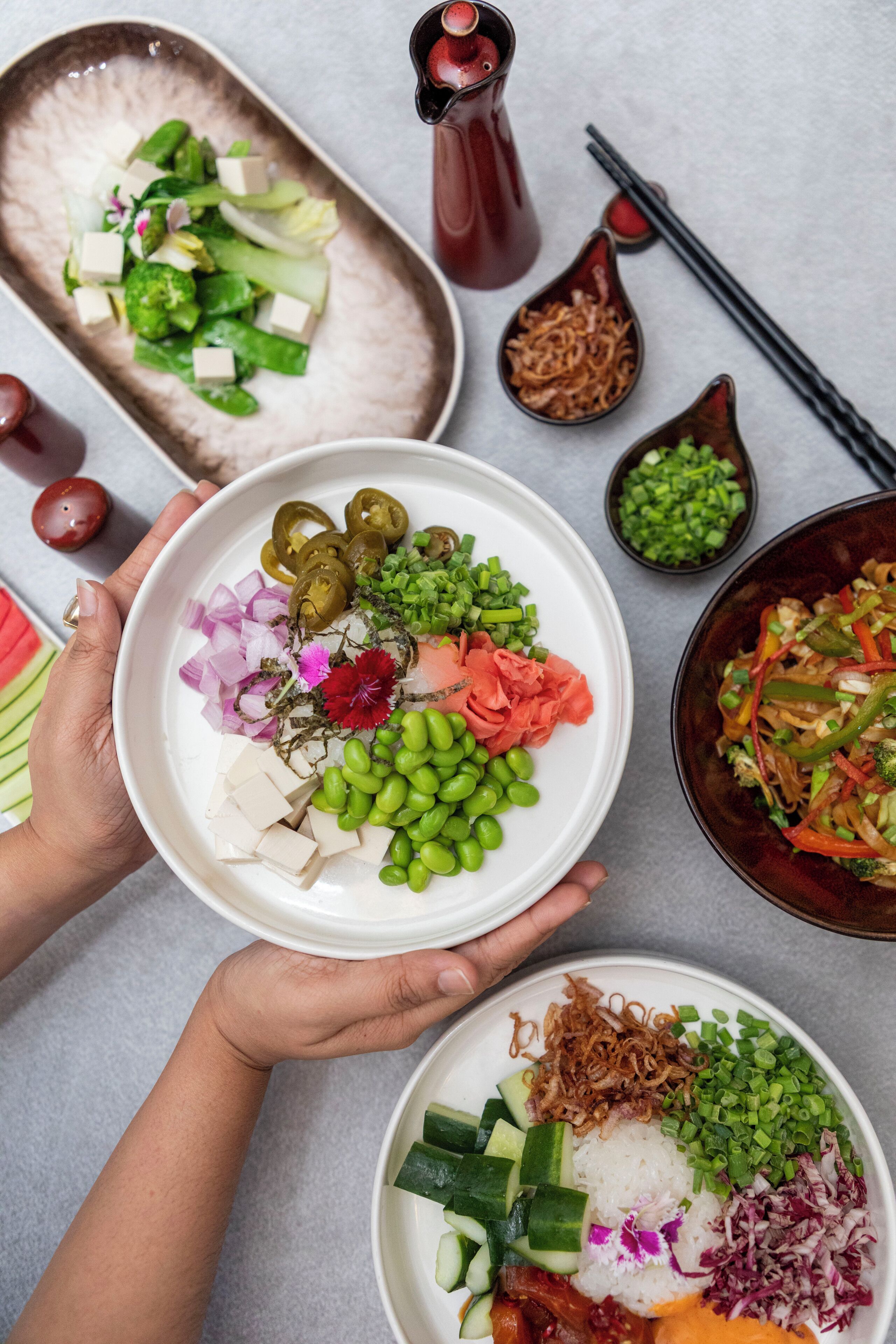 Uma salada em uma tigela com diversos ingredientes, um prato de macarrão e uma travessa de legumes.