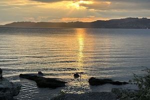 Um lago calmo ao pôr do sol, com o perfil de uma colina ao fundo.