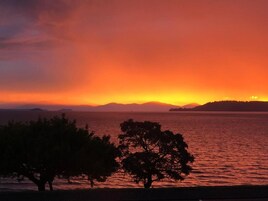 Um pôr do sol sobre a água, com silhuetas de árvores e paisagens distantes.