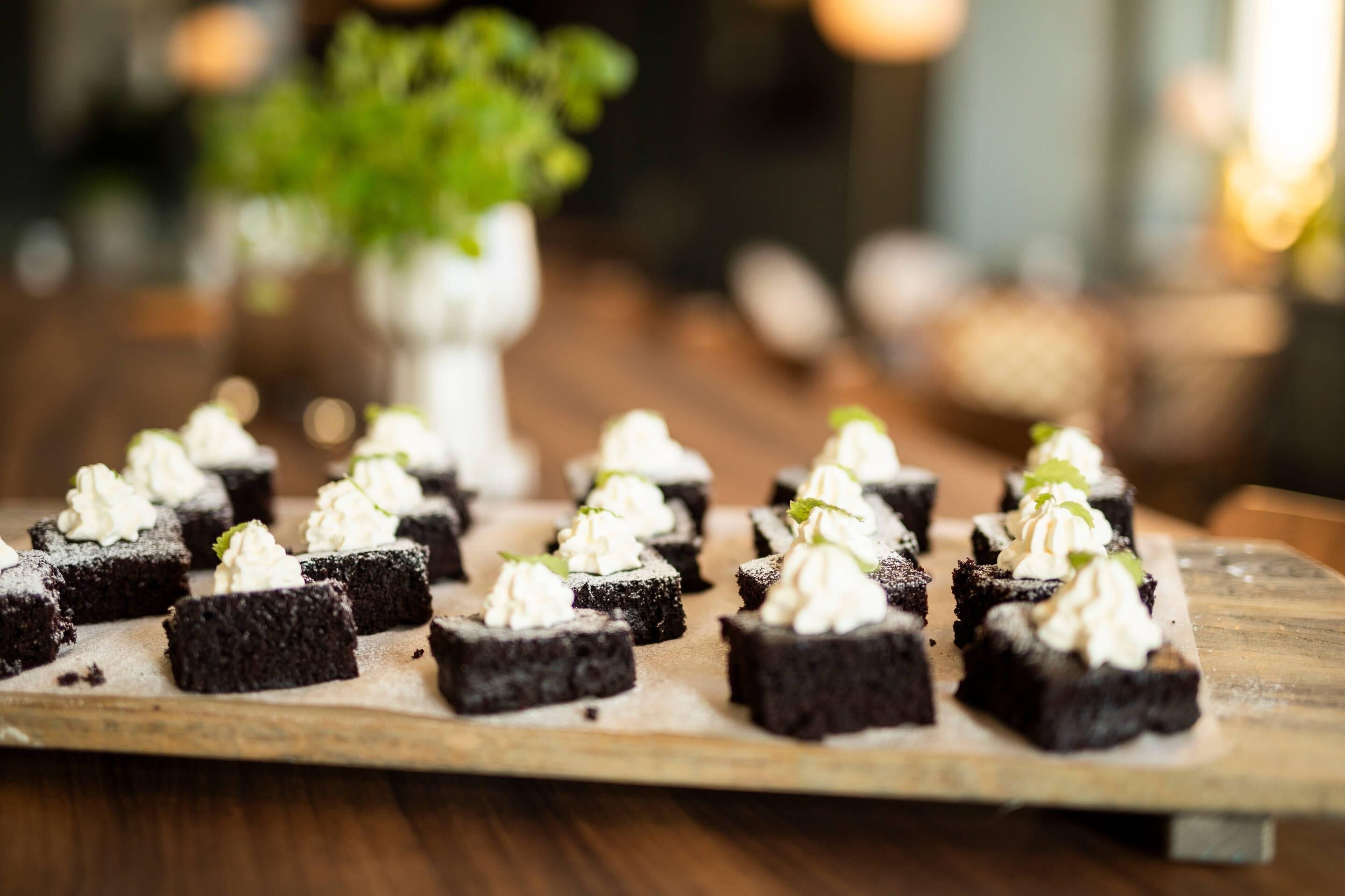Uma tábua de madeira com vários doces quadrados cobertos de chantilly e folhas de hortelã.