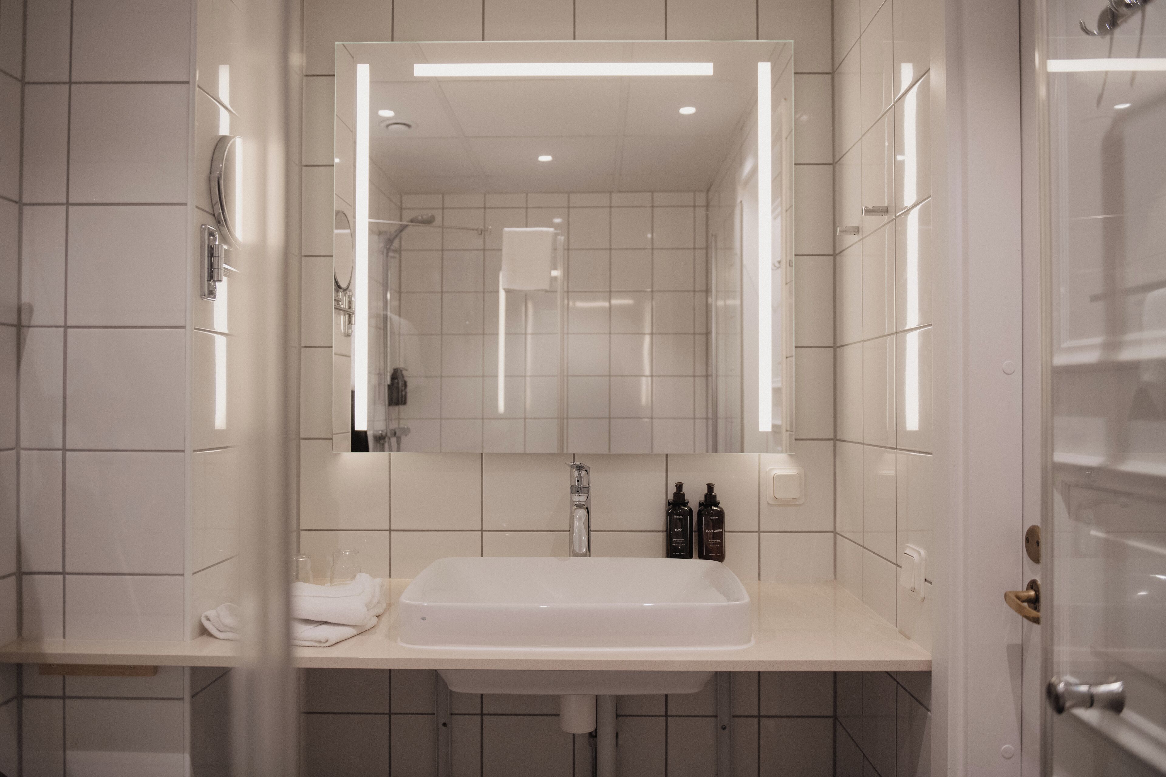 Casa de banho moderna com lavatório branco, espelho e paredes revestidas a azulejos.