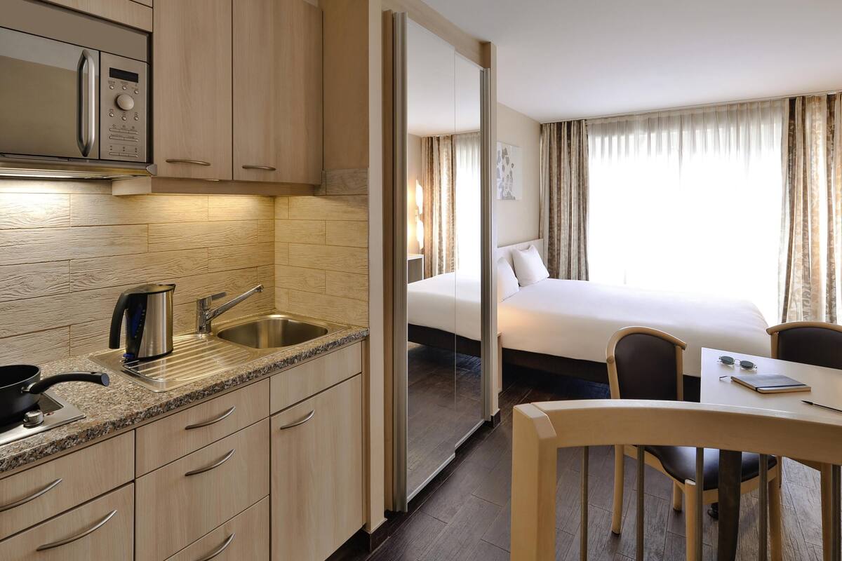 Quarto de hotel moderno com cozinha compacta, cama, área de refeições e vista para o exterior.