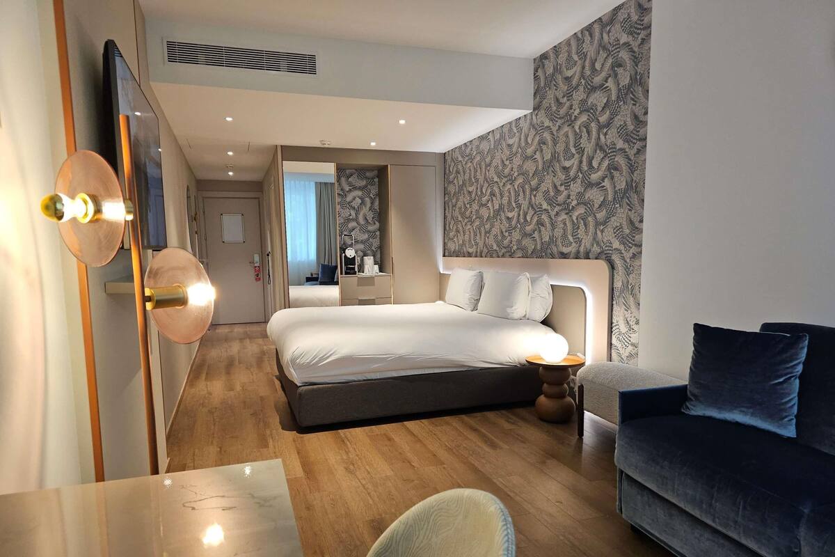 Quarto de hotel moderno com uma cama grande, um sofá, uma escrivaninha e um espelho.