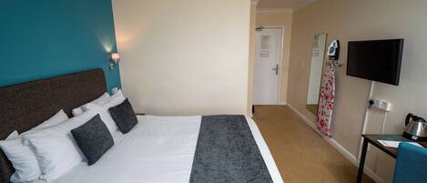 Quarto de hotel com cama, escrivaninha, televisão e porta.