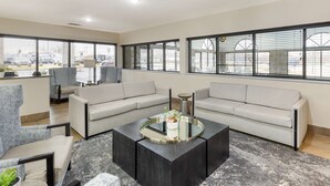 Uma sala de estar moderna com um sofá seccional, uma mesa de centro redonda e grandes janelas com vista para a cidade.