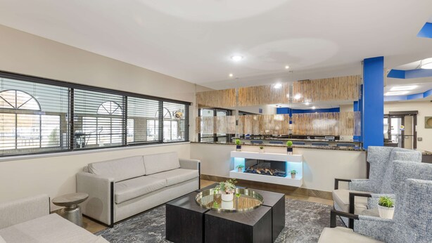 Uma sala de estar moderna com sofá, poltronas, mesa de centro e cozinha ao fundo.