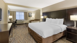 Quarto de hotel com uma cama grande, uma escrivaninha, uma cadeira, uma televisão e uma janela com cortinas.