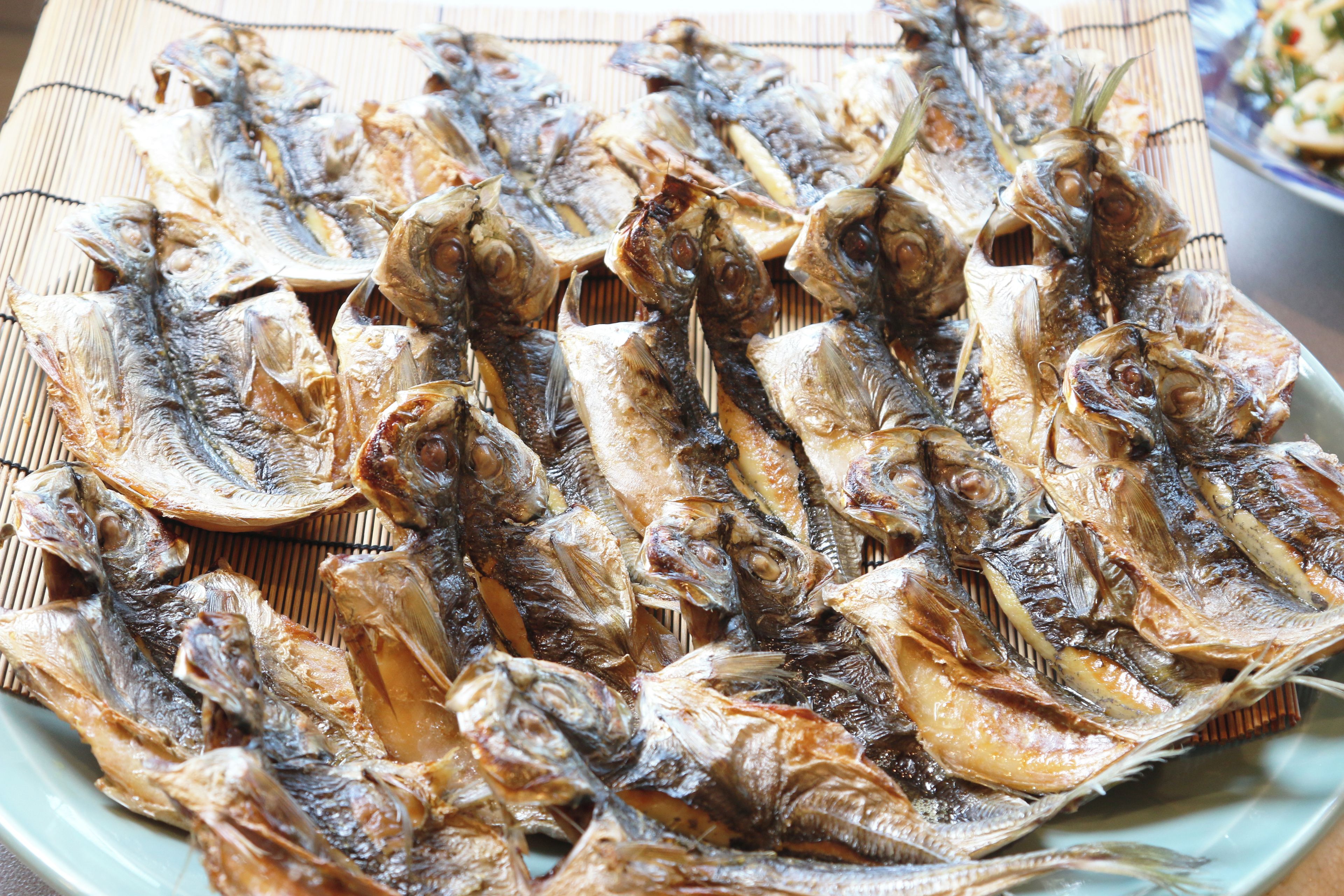 Uma grande travessa de peixe seco disposta sobre um tapete de bambu.