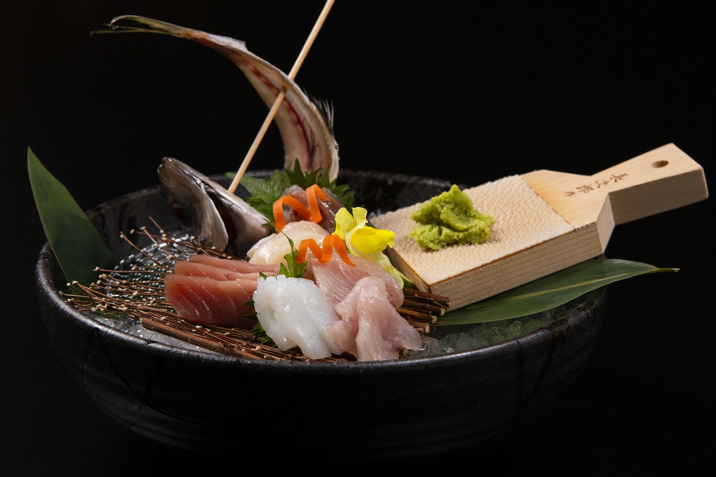 Uma tigela de sashimi com diferentes tipos de peixe, acompanhamentos e uma tábua de servir de madeira.
