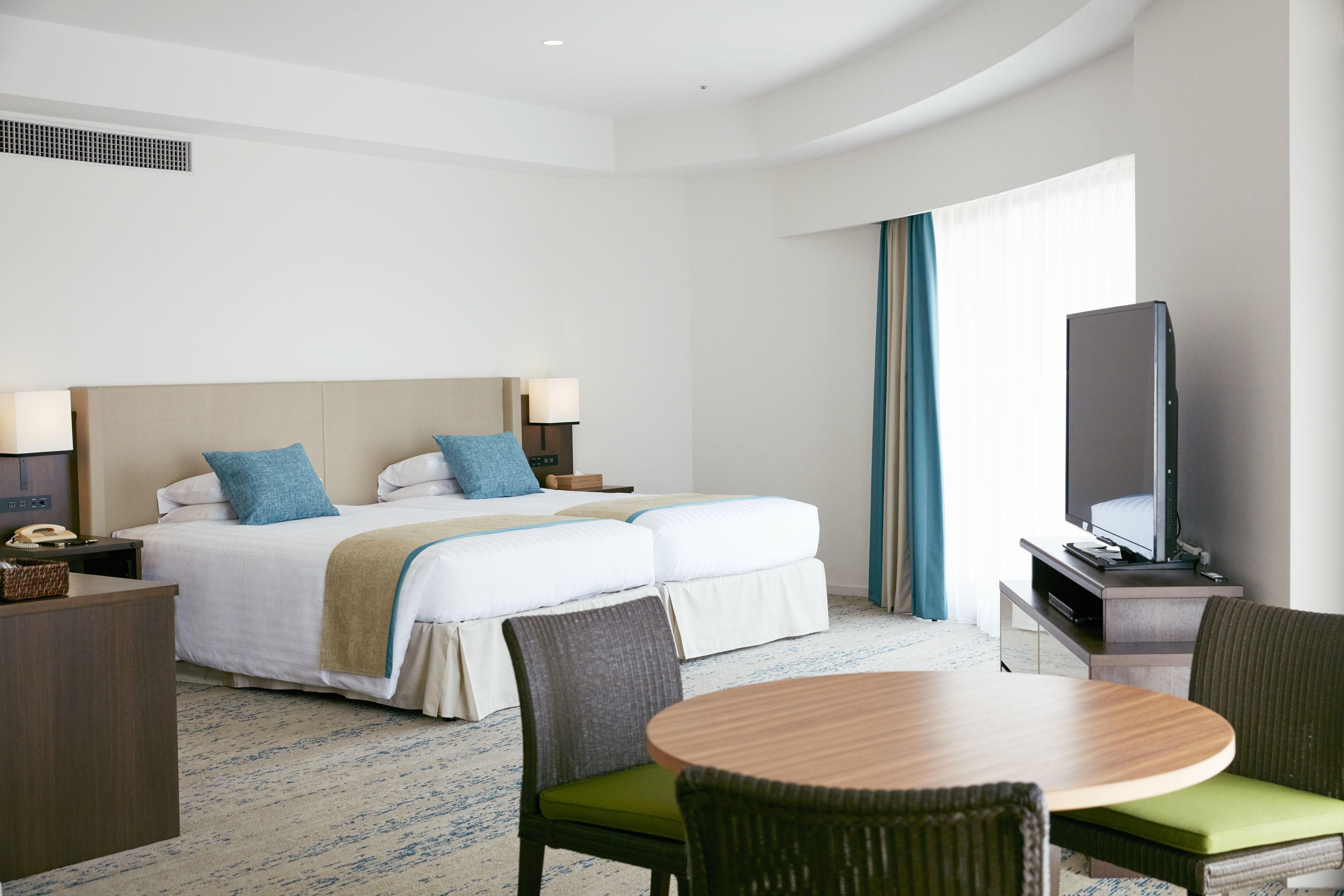 Quarto de hotel com cama, televisão, secretária e mesa de jantar.