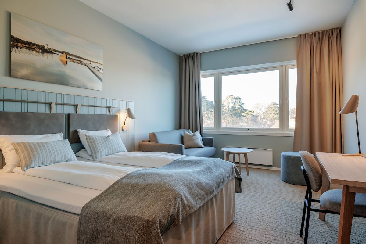 Quarto de hotel com uma cama grande, um sofá, uma mesinha e uma escrivaninha.