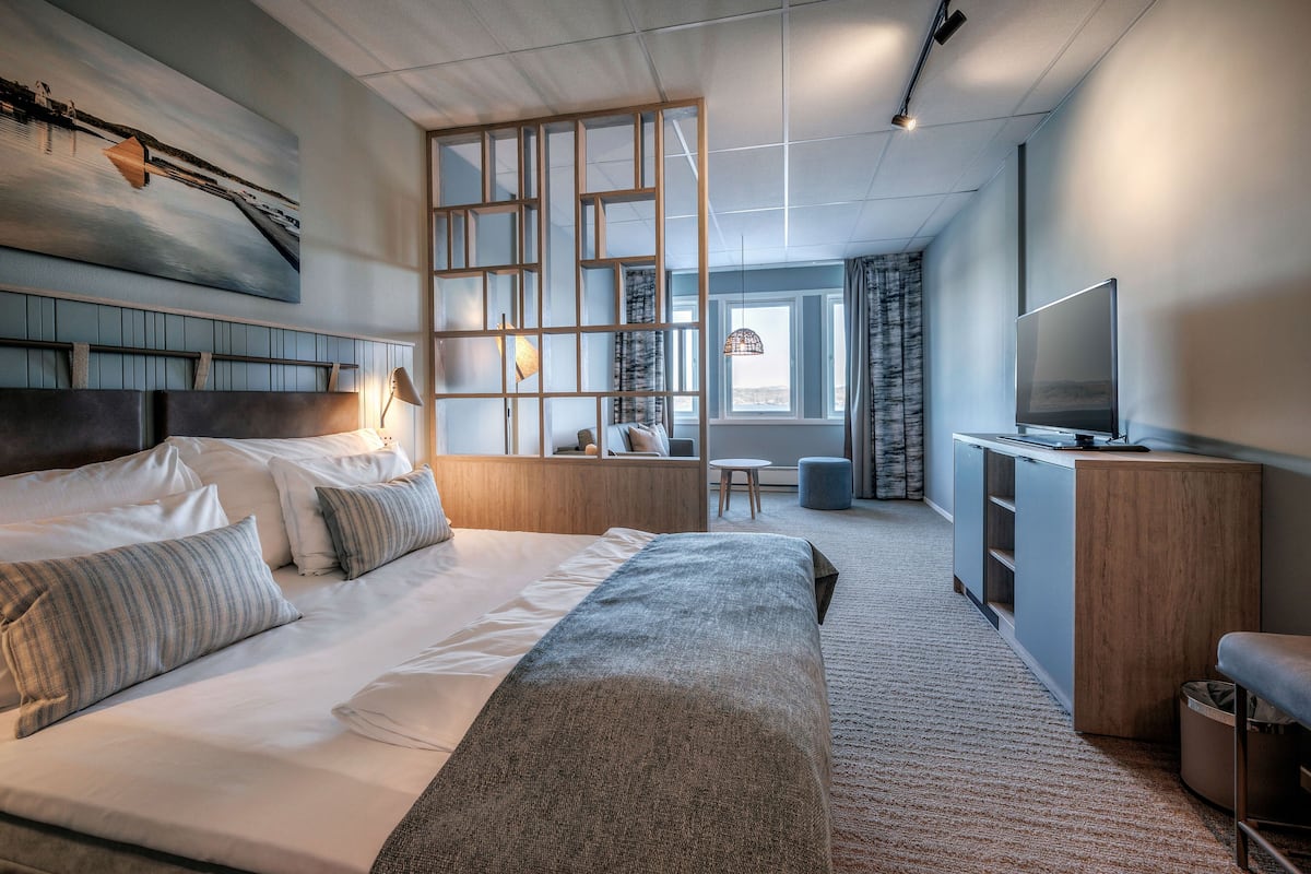 Quarto de hotel moderno com uma cama grande, televisão, área de estar e vista para a cidade.