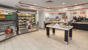 Uma praça de alimentação com áreas refrigeradas para sanduíches, saladas e bebidas frias, e um balcão para refeições e bebidas quentes.