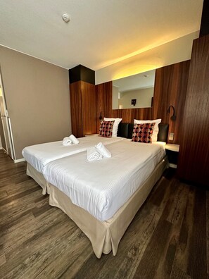 Quarto de hotel com uma cama grande, duas mesas de cabeceira, um espelho e piso de madeira.