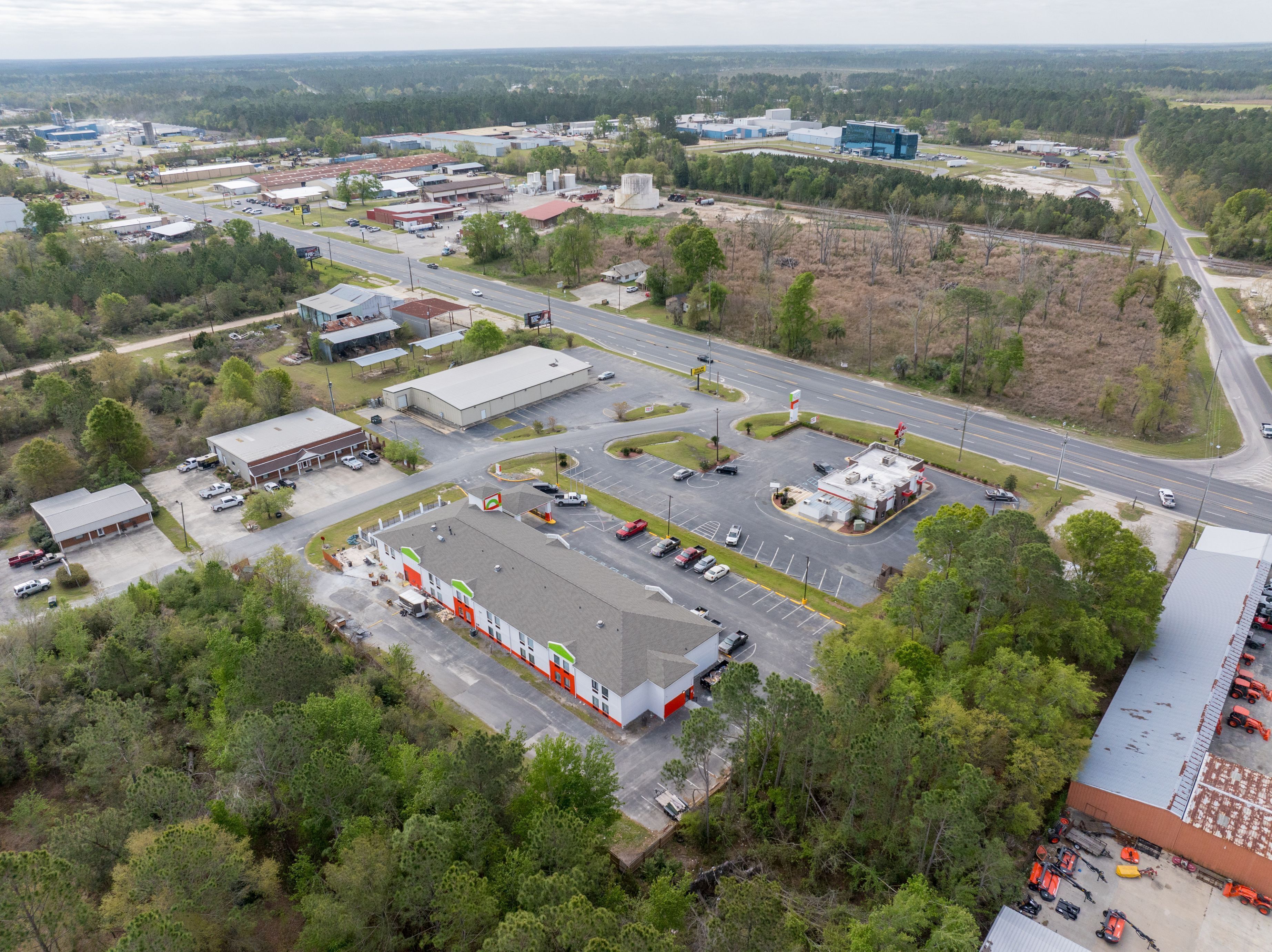 Vista aérea de uma área comercial com vários edifícios, estacionamentos e uma estrada.
