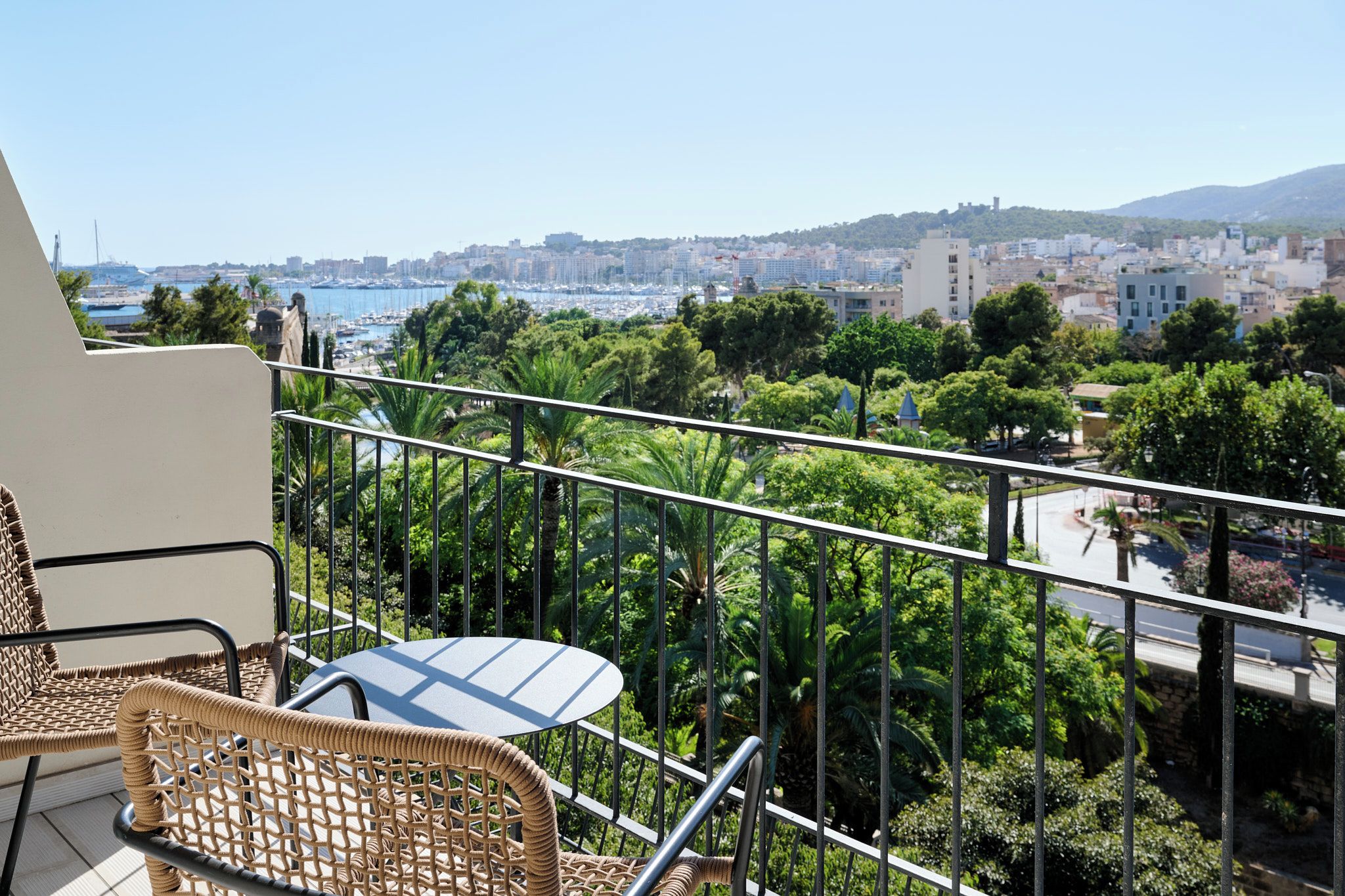 Varanda com cadeira e mesa de vime, com vista para um porto de iates e paisagem urbana.