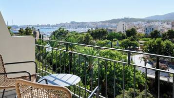 Varanda com cadeira e mesa de vime, com vista para um porto de iates e paisagem urbana.