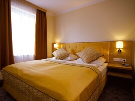 Quarto de hotel com uma cama grande, duas luminárias de cabeceira, uma mesa de apoio e uma janela com cortinas.
