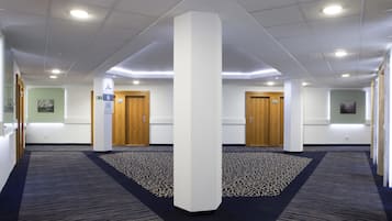Um hall de hotel com piso coberto de carpete, um pilar grande, portas de madeira e uma placa indicando a sala número 6.