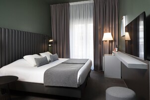 Quarto de hotel moderno com uma cama grande, uma escrivaninha, uma cadeira e um espelho.